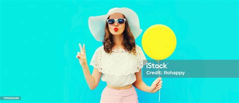 파란 배경에 여름 하얀 밀짚 모자를 쓰고 노란 풍선으로 공기 키스를 보내는 아름다운 젊은 여성의 초상화 25 29세에 대한 스톡 사진 및 기타 이미지 Istock