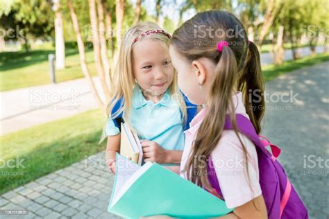 수업 첫날 배낭과 책을 들고 있는 귀여운 학생 소녀 두 명 학생들이 재미있고 야외에서 노트북을 보고 있습니다 학교 개념으로 돌아가기 2명에 대한 스톡 사진 및 기타 이미지