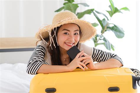 여름 캐주얼 옷과 밀짚 모자에 젊은 아시아 여성의 초상화는 침실에서 노란색 수하물과 미소와 편안한 분위기 그것은 여름 시간에 여행에 갈 시간 노란 가방을 가진 행복한 관광