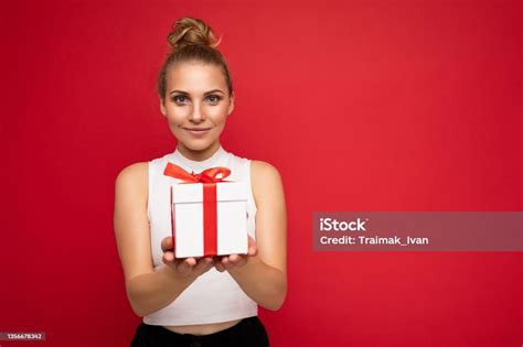 빨간 리본으로 선물 상자를 들고 캐주얼 흰색 상단을 들고 텍스트 복사 공간과 빨간색 배경 벽에 고립 아름다운 매력적인 귀여운 귀여운 젊은 금발 여성의 사진 촬영 생일 컨셉