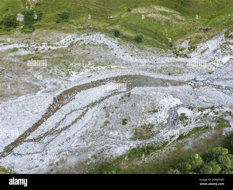 Stony River Bed In High Summer Season Surrounded By Green Alpine
