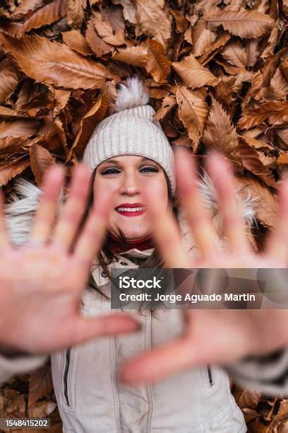 모직 모자를 쓴 젊은 여성이 밤나무 숲의 나뭇잎 담요 위에 누워 웃고 카메라를 바라보며 손을 잡고 있다 가을에 대한 스톡 사진 및 기타 이미지 Istock