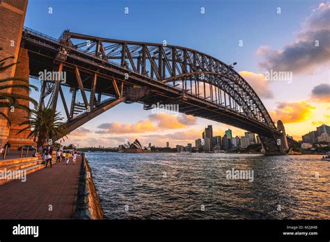 People Walk Under The Harbour Bridge With View Of Sydney Skyline Stock