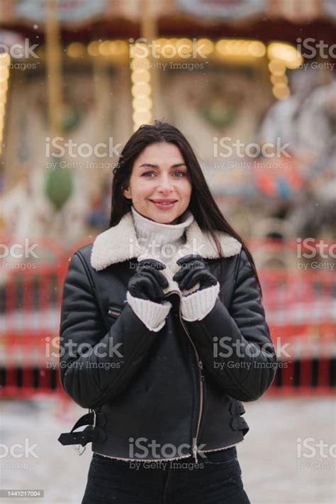 따뜻하고 아늑한 옷을 입은 아름다운 백인 여성이 축제 조명을 배경으로 눈이 내리면서 크리스마스 박람회에서 야외로 걸어갑니다 12월에 대한 스톡 사진 및 기타 이미지 Istock