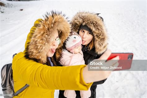 두 백인 여성과 아기 소녀는 그녀의 작은 아이와 그녀의 친구 또는 이모와 함께 셀카를 찍는 어머니 사진을 찍거나 야외에서 눈으로 자연에서 겨울에 휴대 전화를 사용하여 화상