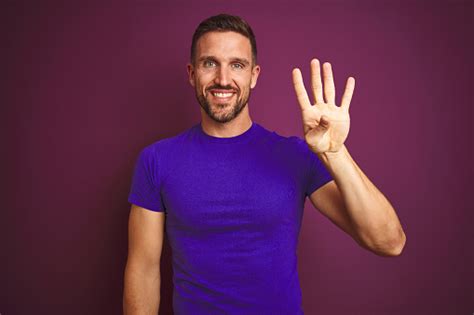 캐주얼 한 보라색 티셔츠를 입은 젊은 남자는 자신감과 행복 미소를 지으면서 손가락 번호 4를 보여주고 가리키는 라일락 고립 된 배경을 보여줍니다 T 셔츠에 대한 스톡 사진