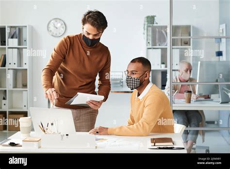 Young Man In Mask Holding Clipboard And Pointing Ar Laptop While