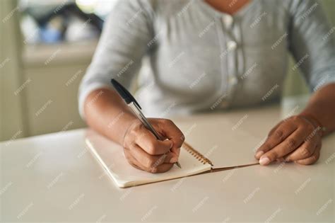 집에 있는 테이블에 앉아 노트북에 글을 쓰는 아프리카계 미국인 여성 무료 사진