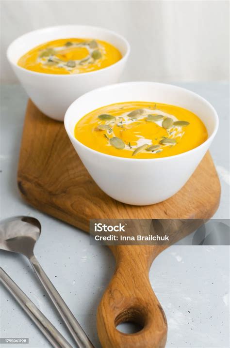 회색 배경의 나무 도마에 말린 씨앗과 백리향 잎을 곁들인 호박 크림 수프 두 그릇 건강한 식생활의 개념 채식주의자 및 비건 음식