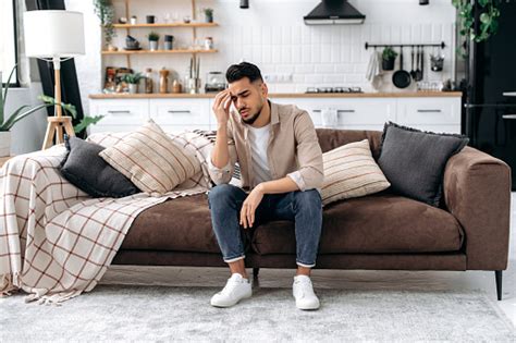 외로움 좌절 된 걱정 혼란스러운 인도 또는 아라비아 청년은 캐주얼 웨어를 입고 거실의 소파에 혼자 앉아 개인적인 문제 걱정 우울증 스트레스를 경험합니다 20 24세에 대한