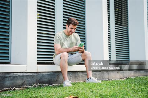 방과 후 대학 캠퍼스에 앉아 핸드폰으로 게임을 하는 젊은 남자 10대 학생이 스마트폰으로 소셜 미디어 앱에 타이핑을 하며 웃고 있다 청년 남자에 대한 스톡 사진 및 기타