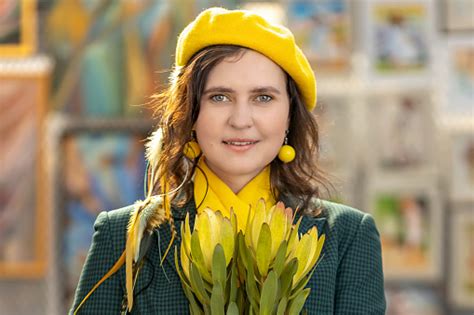 녹색 바지 수트와 노란 베레모를 쓴 젊은 여성이 미술관을 배경으로 노란 봄 꽃 꽃다발을 들고 서 있습니다 봄 휴가의 개념 3 월 8 일 부활절 3월에 대한 스톡 사진 및