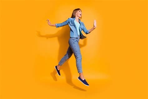 전체 길이 몸 크기 사진 비행 높은 점프에 놀라운 이빨 미소 아름 다운 노란색 배경에 고립 된 그녀가 숙 녀 건강 한 라이프 스타일 캐주얼 청바지 데님 셔츠 옷 입고 조깅