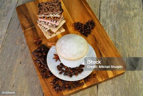 나무 도마위에 서 있는 흰색 도자기 카푸치노 컵의 최고 전망 다양한 종류의 초콜릿 조각 계피 스틱 스타 아니스 하트 모양의 커피 콩이 나란히 놓여 있습니다 0명에 대한 스톡