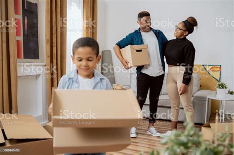 행복한 작은 아프리카 계 미국인 소년은 골판지 상자를 들고 젊은 가족은 구입 한 아파트로 이동 흥분 아들은 개인 소지품을 운반 부모는 서로 자랑스럽게 보고 가득 찬에 대한
