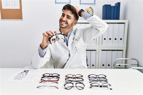 Young Optician Man Holding Optometry Glasses Smiling Confident Touching Hair With Hand Up