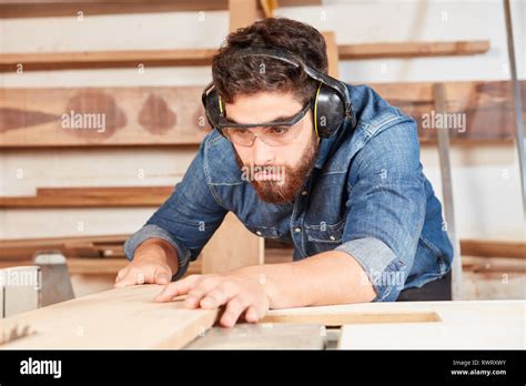 Man As A Carpenter In The Workshop Concentrates Sawing Wood With The