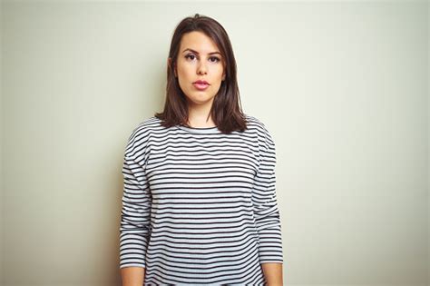 젊은 아름 다운 갈색 머리 여자 얼굴에 심각한 표정흰색 고립 된 배경 에 줄무늬 스웨터를 입고 카메라를 보는 간단하고 자연스러운 갈색 머리에 대한 스톡 사진 및 기타 이미지
