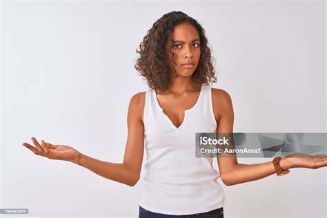 캐주얼 한 티셔츠를 입고 고립 된 흰색 배경에 서있는 젊은 브라질 여성은 단서가없고 팔을 벌려 혼란스러워하고 아무 생각도 개념이 없습니다 T 셔츠에 대한 스톡 사진 및 기타
