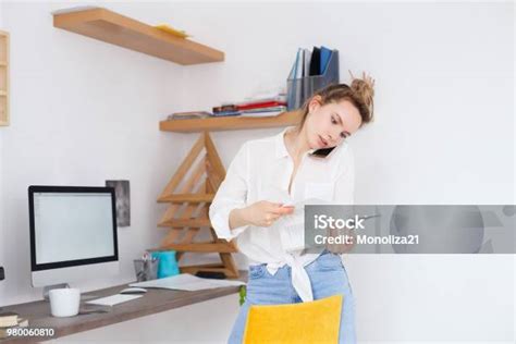 컴퓨터와 책상 근처에 서 빛 아늑한 사무실에서 젊은 프리랜서 작업 스마트폰 및 잡지 카탈로그에서 정보에 대 한 검색을 말한다 가정 생활에 대한 스톡 사진 및 기타 이미지