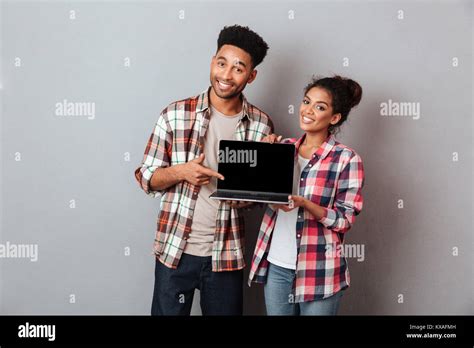 Portrait Of A Smiling Young African Couple Showing Blank Screen Laptop