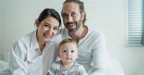 백인 행복한 가족의 초상화 침실에서 카메라를 봐 젊은 매력적인 부부 부모 아버지와 어머니는 어린 남자 아이와 함께 침대에 앉아 집에서 아침 기상 활동을 즐깁니다 사진