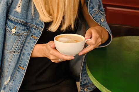 아로마 커피 한 잔을 손에 들고 있는 여성은 레스토랑의 여름 테라스에 앉아 있습니다 소녀는 아침 식사 후 커피를 마십니다 화이트 컵에 맛있는 핫 라떼 조용한 프리랜서 라이프