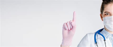 흰색 코트와 분홍색 멸균 장갑을 입은 젊은 아름다운 여성 의사의 자른 모습은 흰색 배경에 손가락주의가있는 표지판을 보여줍니다