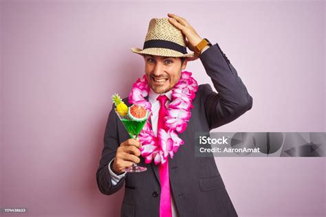 양복 모자 하와이안 레이 를 입고 칵테일을 마시고 고립 된 분홍색 배경 위에 머리에 손으로 스트레스를 받고 수치심과 깜짝 얼굴에 충격을 받고 화가 났습니다 실수에 대한