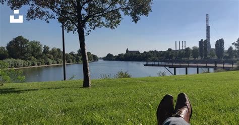 검은 바지와 갈색 가죽 신발을 신은 사람이 물가 근처 잔디밭에 앉아 있습니다 사진 Unsplash의 무료 부다페스트 이미지