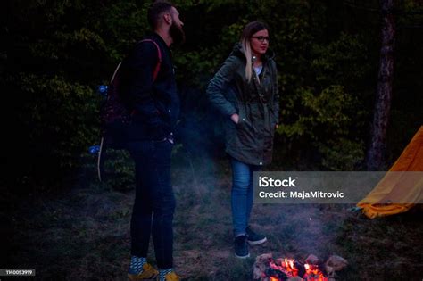 아름 다운 커플 앉아있는 캠프 파이어 주위에 캠핑 텐트와 배경에 남자는 막대기로 불을 긋기도 합니다 관광에 대한 스톡 사진 및 기타 이미지 Istock
