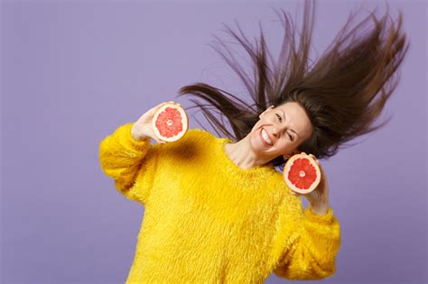 보라색 파스텔 배경에 고립 된 신선한 익은 자 몽의 Halfs를 들고 비행 머리와 모피 스웨터에서 쾌활 한 젊은 여자 사람들은 생생한 라이프 스타일 휴식 휴가 개념입니다