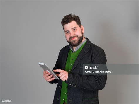 검은 머리와 전통적인 의상을 입은 수염을 가진 젊은 남자가 회색 배경 앞에 서서 태블릿에서 작동합니다 고급에 대한 스톡 사진 및 기타 이미지 Istock
