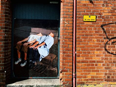 흰색 드레스 셔츠와 검은 바지를 입은 남자가 갈색 벽돌 벽에 앉아 있다 사진 Unsplash의 무료 도시 이미지