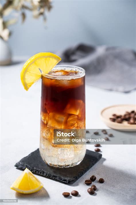 커피 콩과 과일이 있는 밝은 파란색 배경에 얼음과 레몬이 있는 키가 큰 유리잔에 강장제가 든 커피 트렌디 한 여름 공예 상쾌한