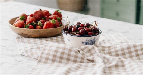 대리석 상판이 있는 주방 섬의 테이블 천에 체리와 딸기로 가득 찬 그릇 한 쌍 흐릿한 배경의 녹색 빈티지 가구 꽃으로 가득 찬 짠 바구니 수직 샷 사진