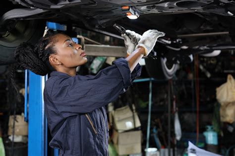 제복을 입은 여성 기술자 자동차 정비사가 정비소에서 정비를 하고 있다 손전등과 렌치 고정 고장 차량을 사용하는 작업자 자동차