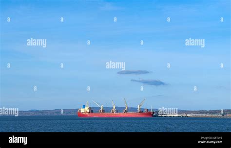 A Large Cargo Ship With A Red Hull And White Superstructure Docked At A