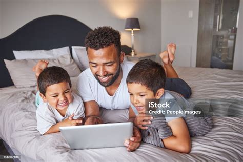 기술 남자와 아이들은 함께 침대에서 휴식을 취하여 주말에 디지털 태블릿으로 유대감을 느끼고 재미있게 지냅니다 행복한 아버지는 유대감 관계를 위해 가족 집에서 아이들과 양질의