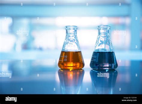 Two Glass Flasks With Orange And Black Solution In Chemical Science Laboratory Background Stock