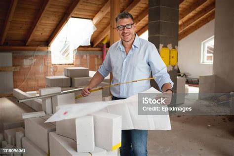 안경과 파란색 셔츠를 입은 남성 건축가가 다락방 의 건설 현장에서 건축 계획을 검토합니다 로프트 아파트에 대한 스톡 사진 및 기타 이미지 로프트 아파트 다락방