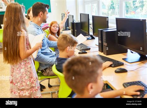 Male And Female Elementary Students Discussing With Teacher In Computer
