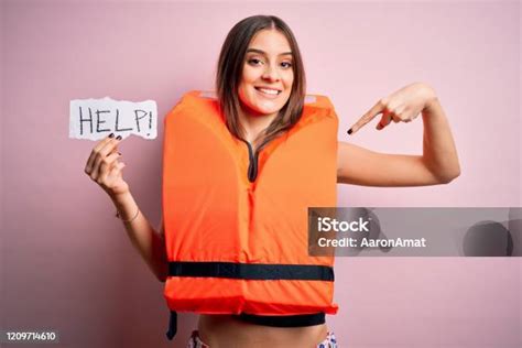 젊은 아름다운 갈색 머리 여자 착용 구명 조끼 들고 종이 와 도움 단어 메시지 와 깜짝 얼굴 가리키는 손가락 에 자신 가리키기에 대한 스톡 사진 및 기타 이미지 Istock