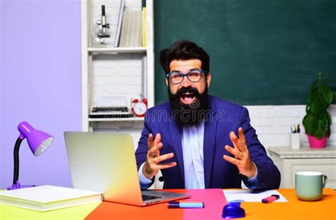 Happy Male School Teacher Or University Professor In Classroom At Desk