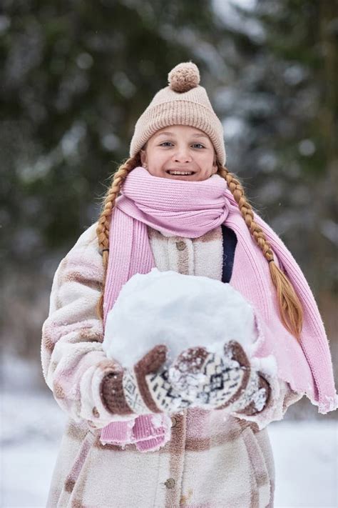 cute cheerful pre teen girl with big snowball on palms looking at