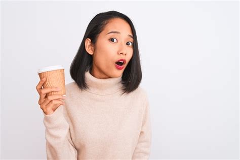 젊은 아름다운 중국 여자 마시는 종이 유리 의 커피 위에 고립 된 흰색 배경 무서워 충격으로 충격으로 깜짝 얼굴 두려움과 두려움 표정으로 흥분 갈색 머리에 대한 스톡 사진