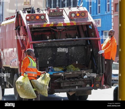 Garbage Truck And Dustbin Men Loading Trash Bags Into The Parked