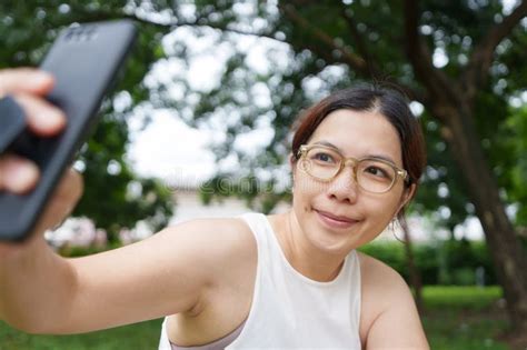 Smiling Asian Woman Wearing Eyeglasses Taking A Selfie Outdoors Stock