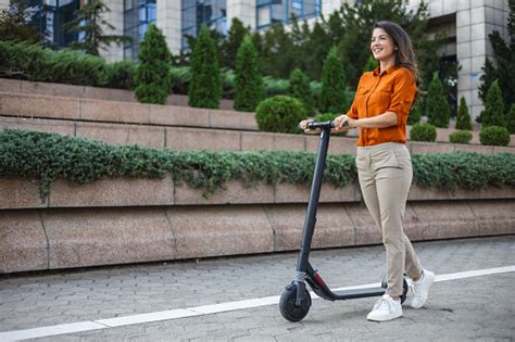 화창한 날에 도시 공원 근처에서 전기 스쿠터를 타고 출퇴근하는 웃는 여성 사업가의 측면 모습 전기 스쿠터에 대한 스톡 사진 및