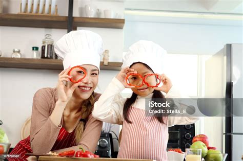 앞치마 요리사 모자를 들고 주방에서 건강한 식사를 요리하는 동안 잘린 피망을 씌우는 행복한 아시아 엄마와 딸 음식을 요리하는 사랑스러운 가족 요리사 엄마와 아이가 함께